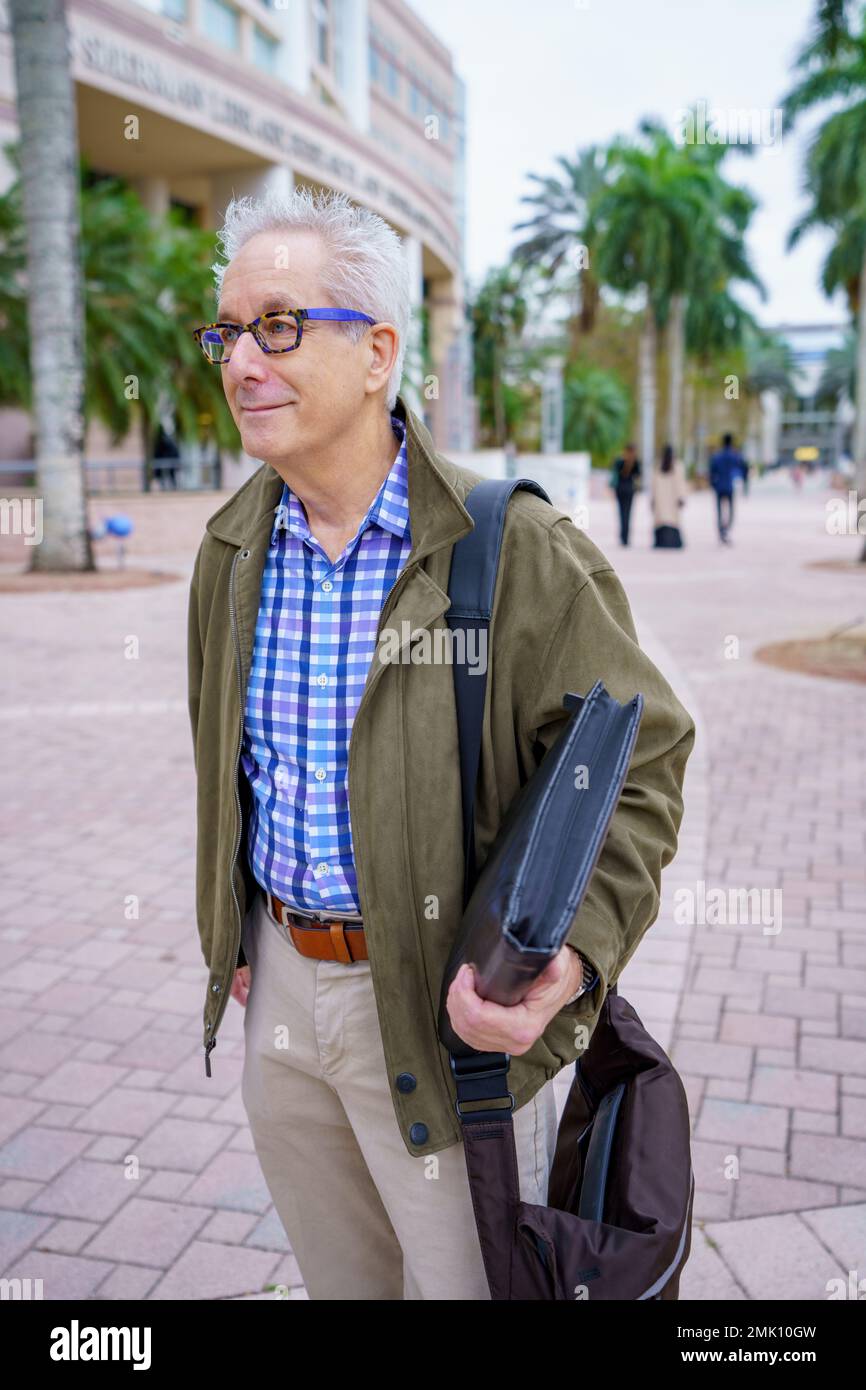 PHoto of a college professor walking on campus with blurry people in ...