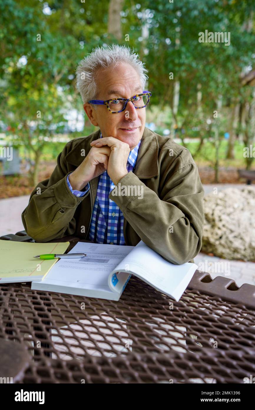 College university professor sitting on a table reading a text book ...