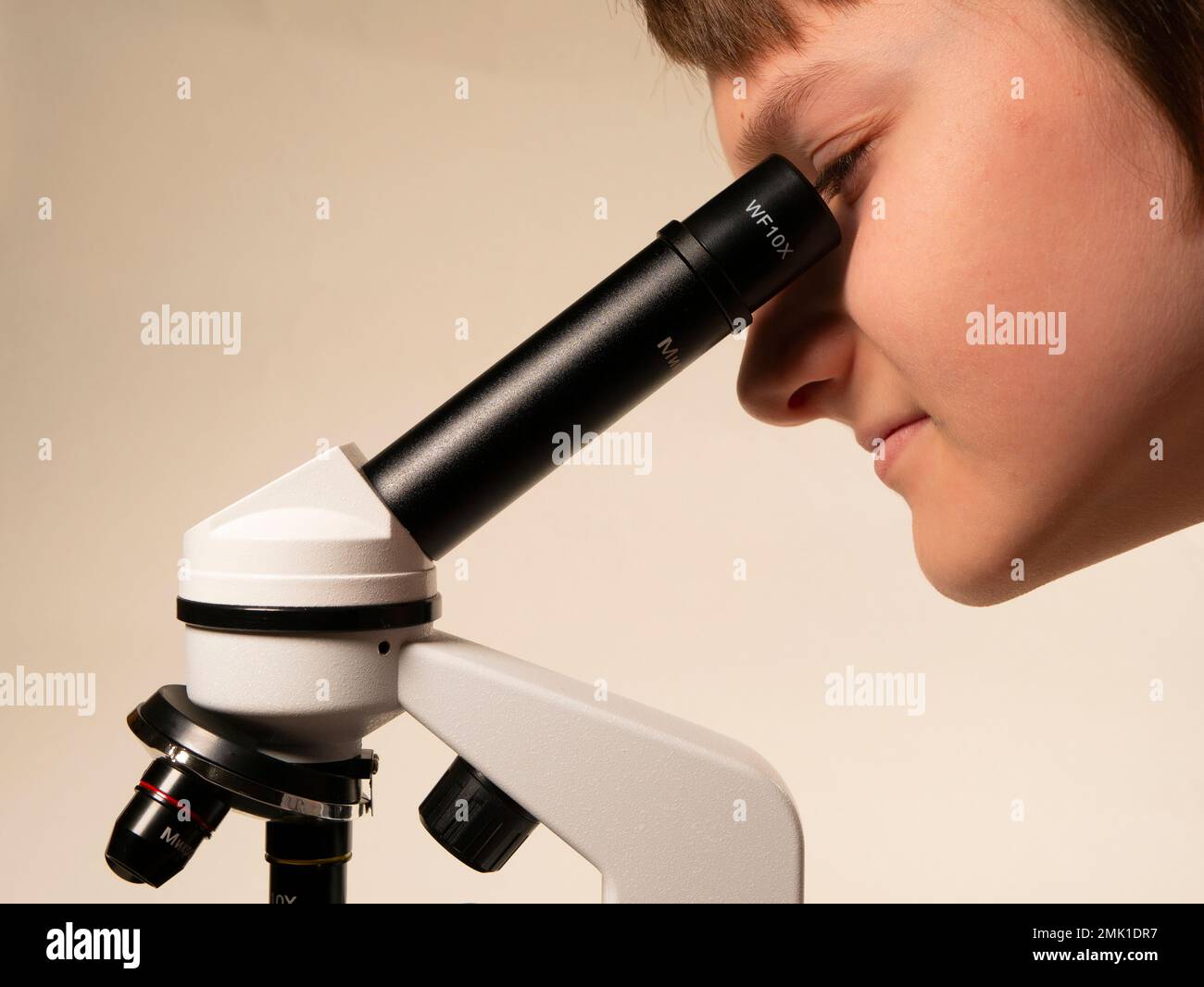 The child looks into the eyepiece of a microscope on a white background ...