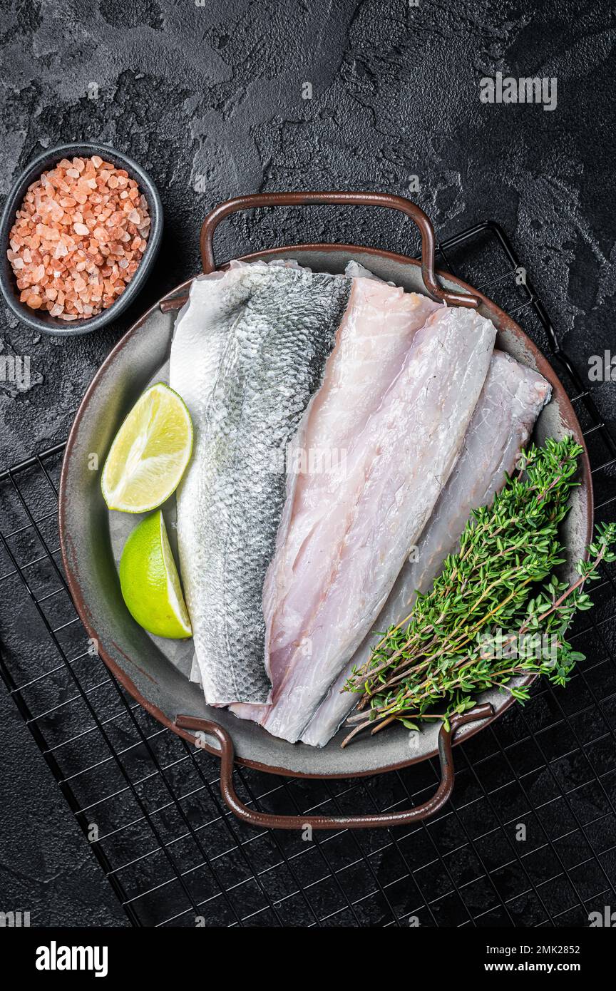 Raw Sea Bass fillet, Labrax fish with herbs and lime. Black background ...
