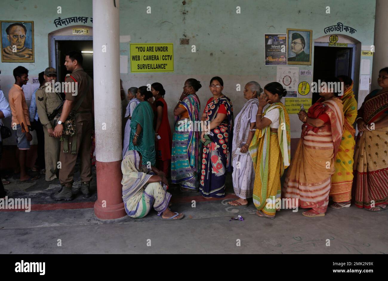Indian men and women stand in queue to cast their votes at a polling ...