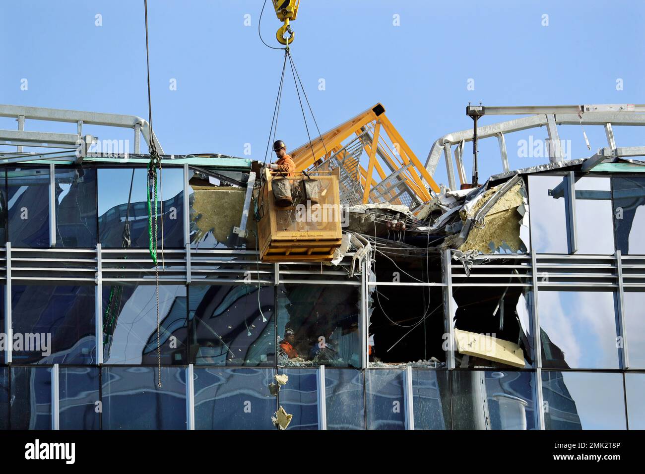 With a portion of the broken crane on the roof behind, a worker ...