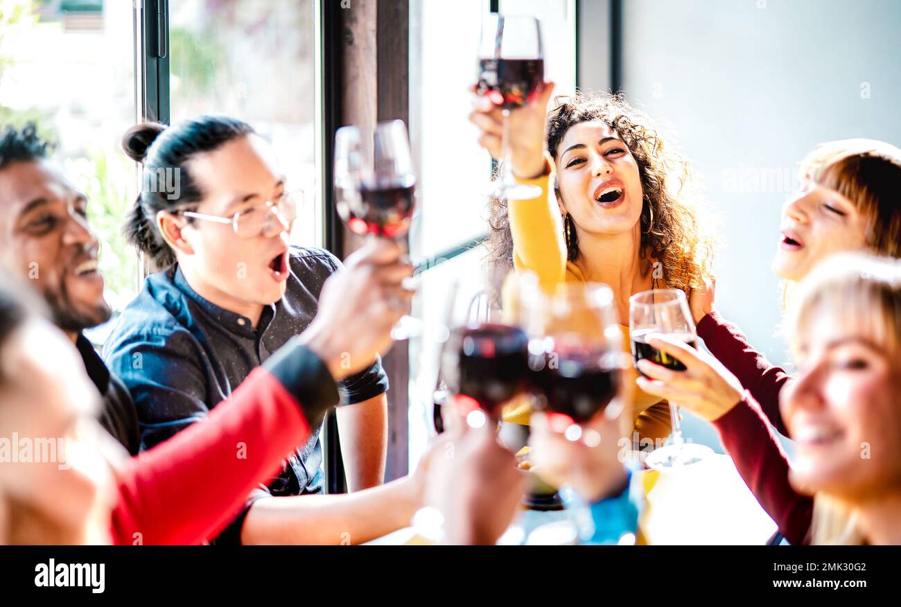 Young multicultural friends drinking and toasting red wine at dinner ...