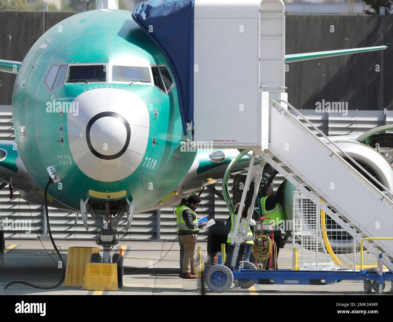 Workers stand near an engine on a Boeing 737 MAX 8 airplane being built ...
