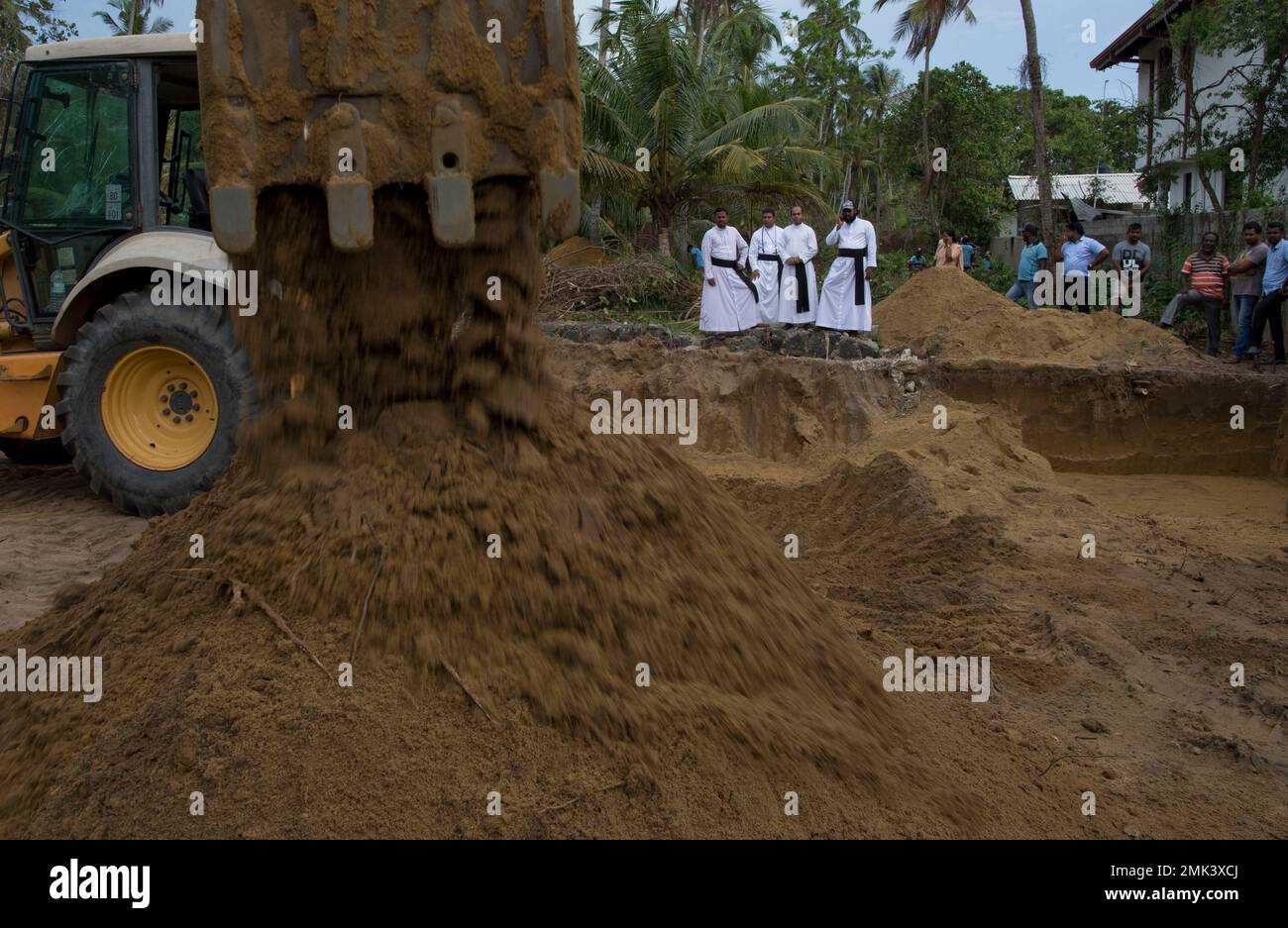 Clergymen watch as an earth mover is used to prepare ground for a mass ...