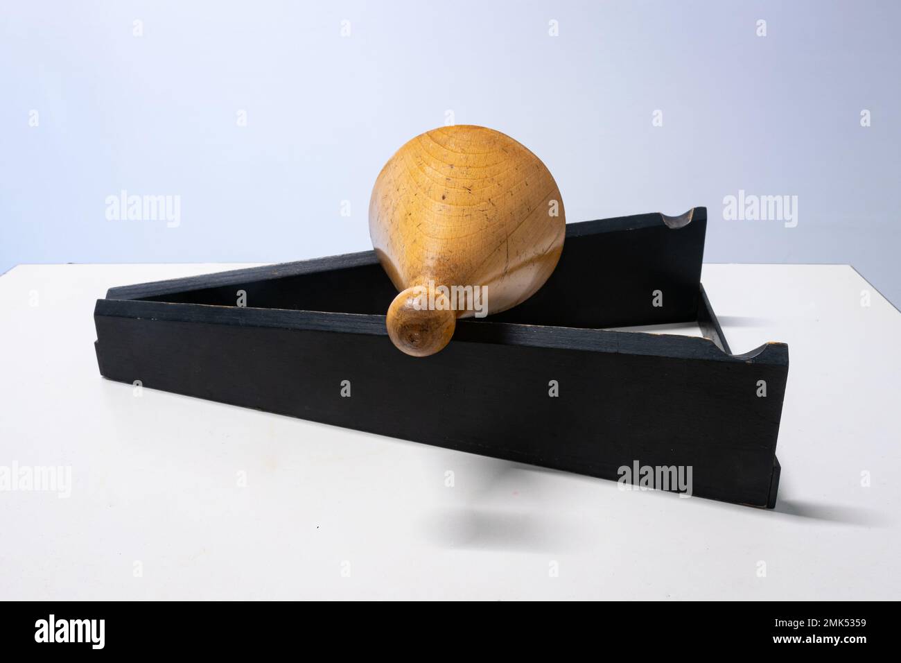 A wooden double cone lies on a slope and rolls upward, seemingly ...