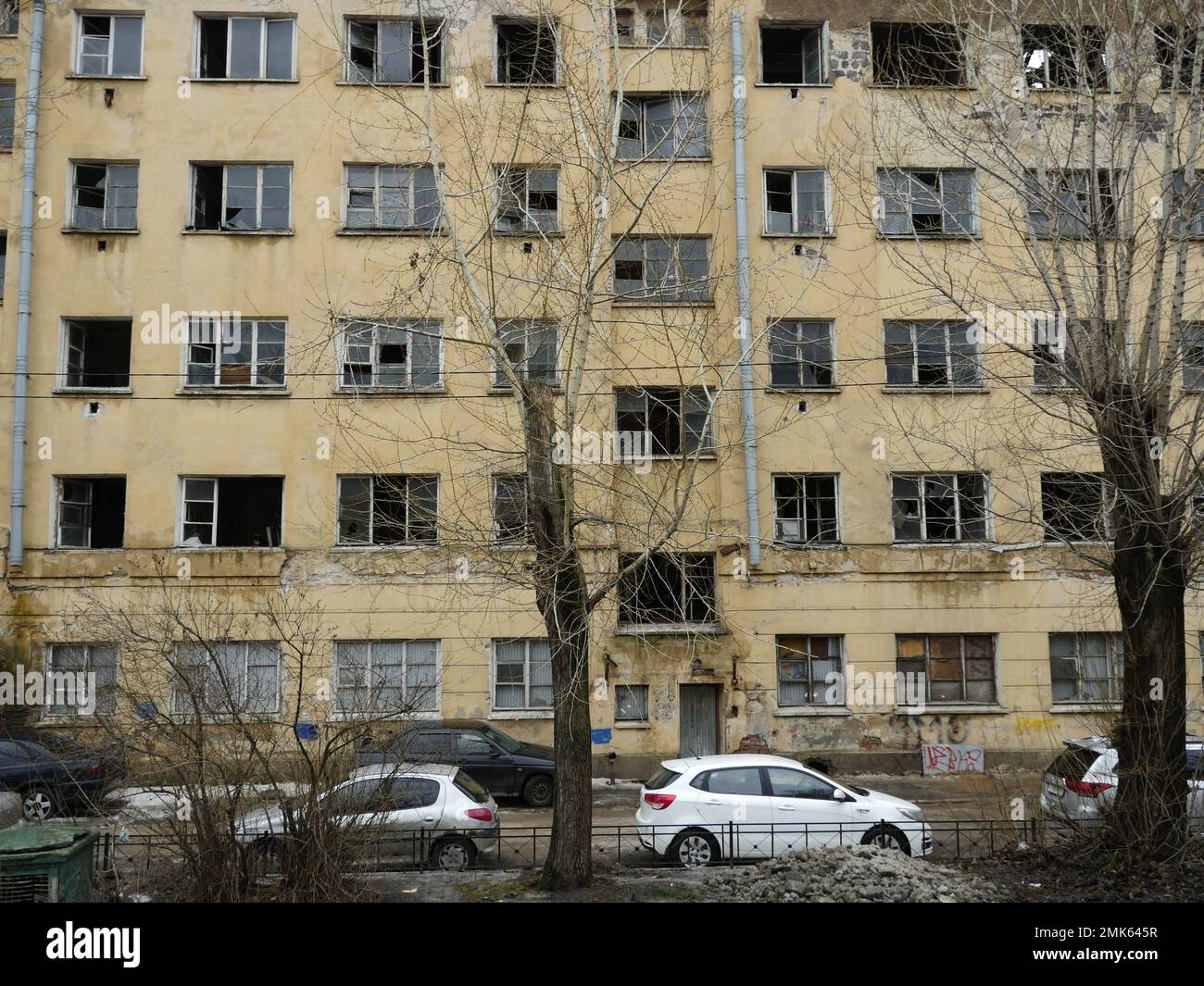 building with broken windows and a hole in the roof, cars of residents ...