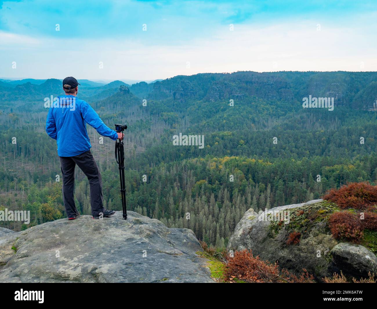 Photographer with folded tripod on end of cliff thinking. NAtural ...