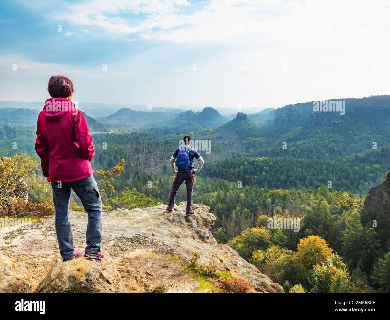 Boy and girl tourists stay on cliff and thinking. Forest in valley with ...