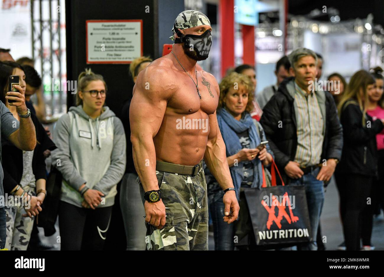 Visitors look at a tall bodybuilder in the fair halls at the world's ...