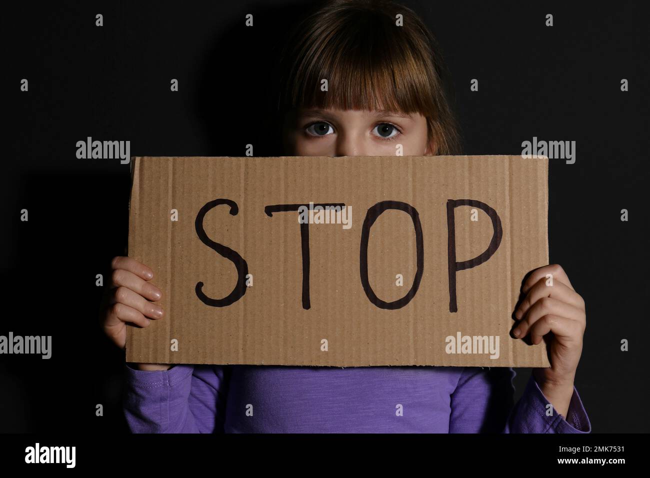 Abused little girl with sign STOP near black wall. Domestic violence ...