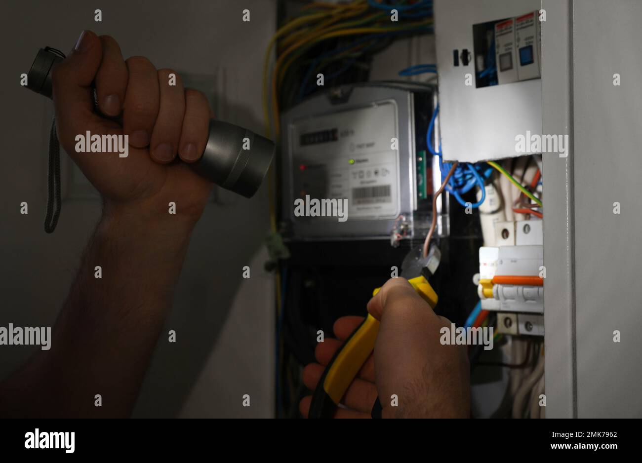 Electrician with flashlight fixing electric panel indoors, closeup ...