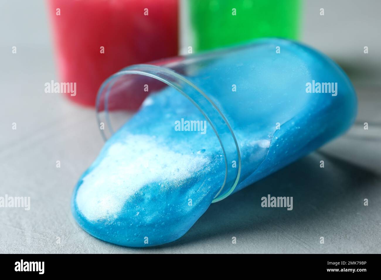 Overturned plastic container with light blue slime on grey background ...