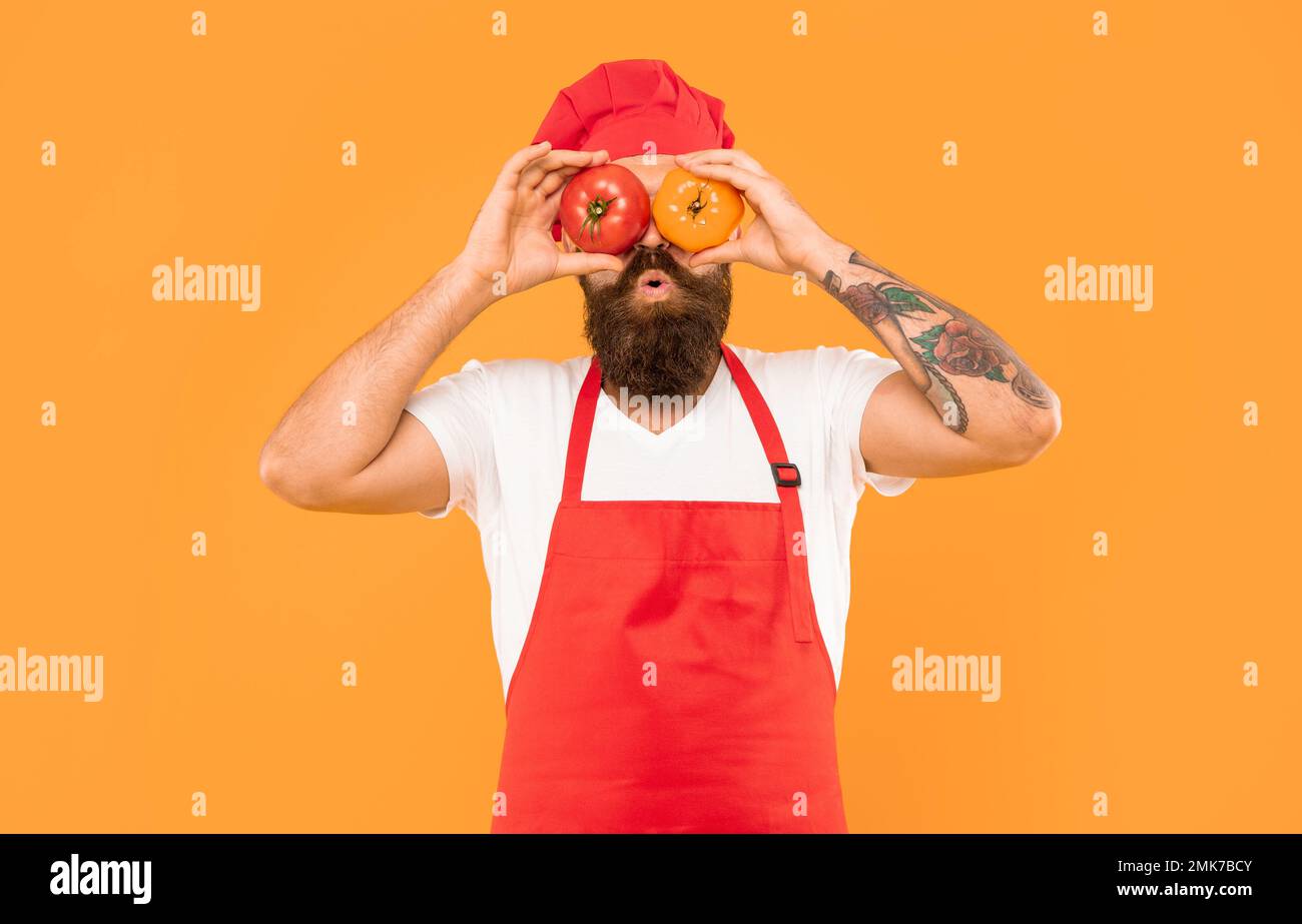 Surprised man in cooking apron and toque holding tomatoes on eyes ...