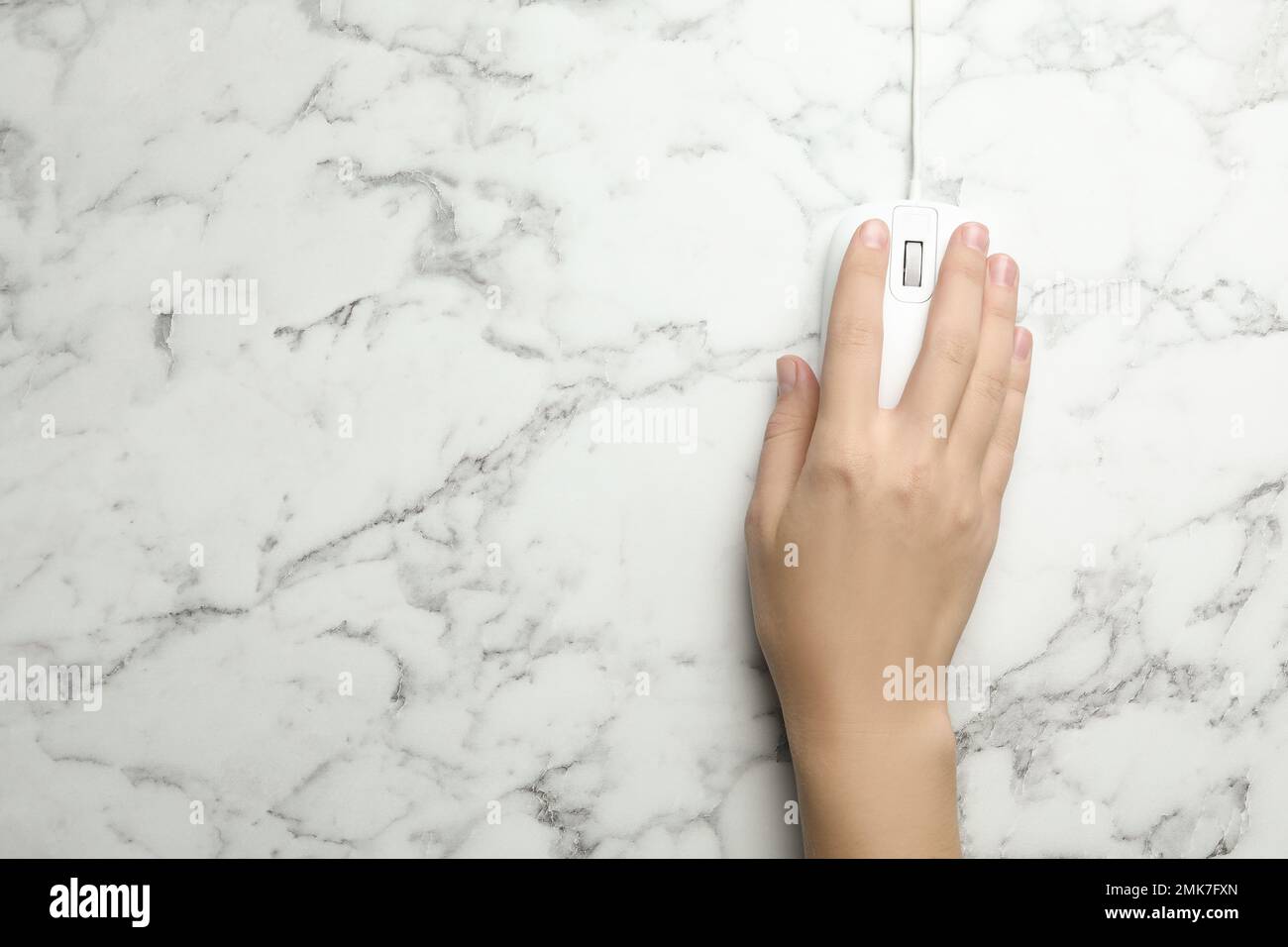 Woman using wired computer mouse on marble table, top view. Space for ...