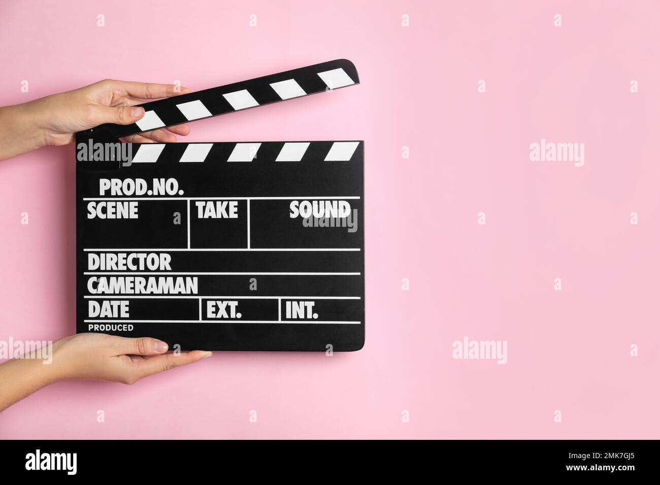 Woman holding clapperboard on pink background, closeup with space for ...