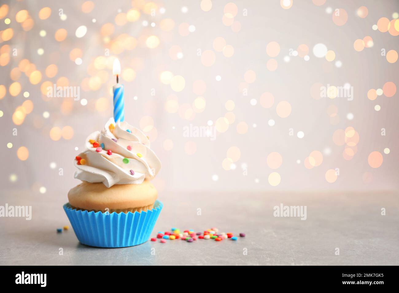 Birthday cupcake with candle on light table, space for text. Bokeh ...