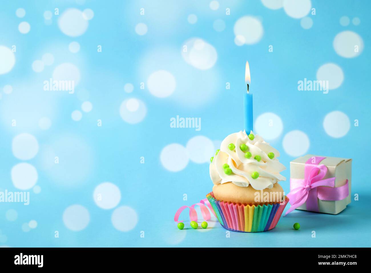 Birthday cupcake with candle and gift box on light blue background ...
