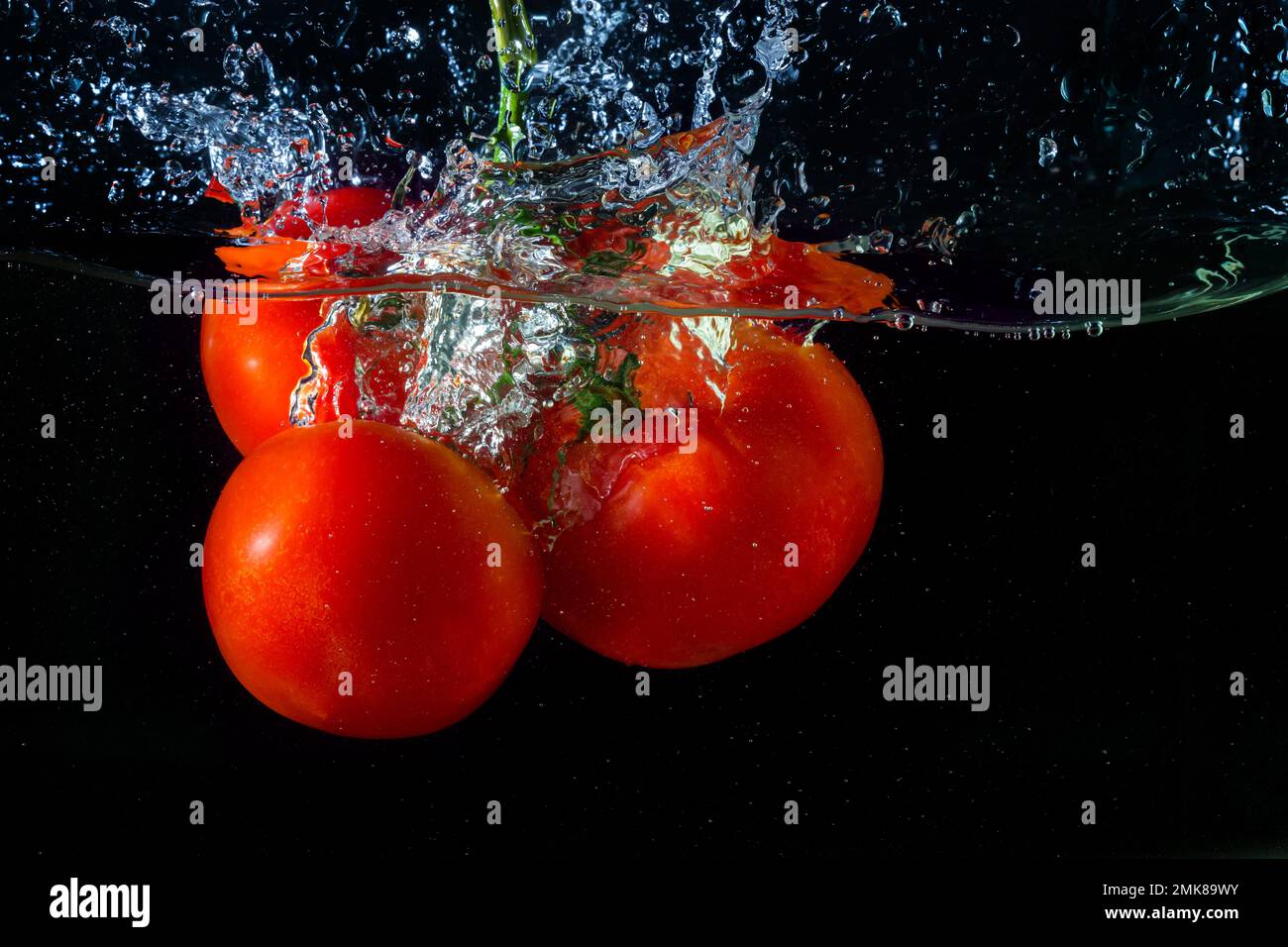 Fresh red tomato falling into water with water splash and air bubbles ...