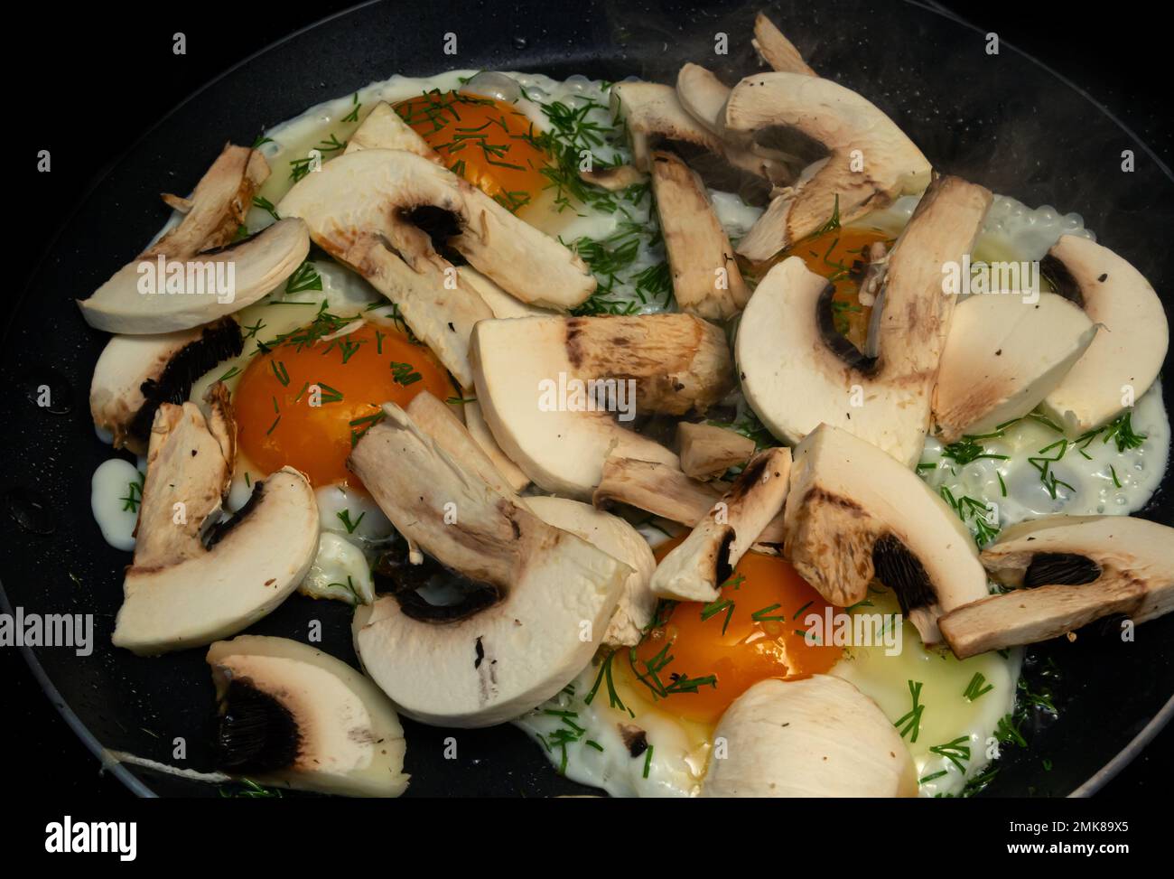 Fried mushrooms and eggs in a pan. The process of cooking breakfast ...