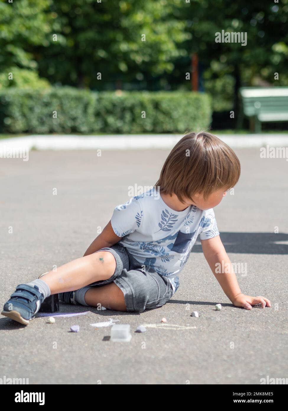Little mindful kid sits on pavement in park. Kid is drawing something ...