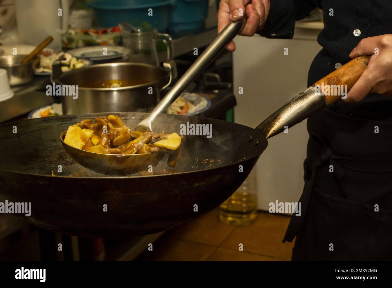 Hands of an Asian chef stir frying a wok beef with bamboo in the ...