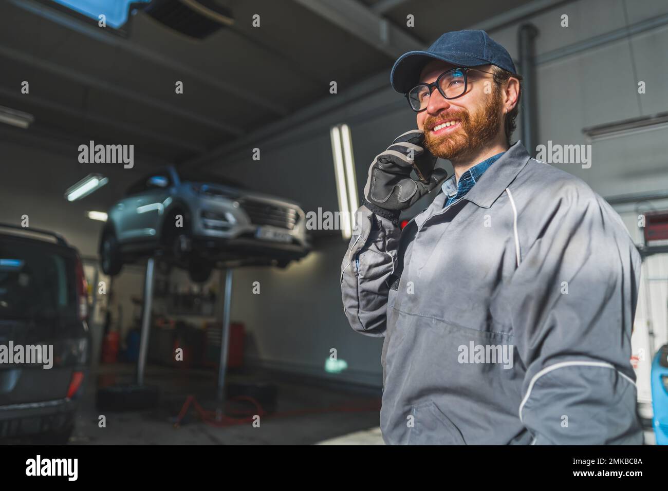 A car mechanic in a grey jacket at an auto repair shop with lifted cars ...