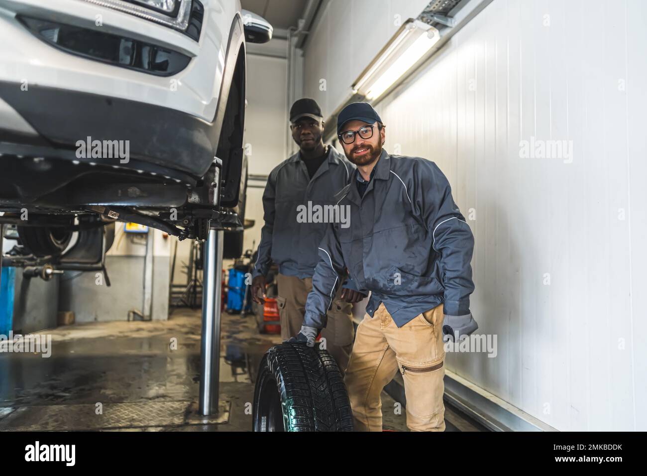 Car mechanics near a lifted white luxury car replacing wheels in a ...