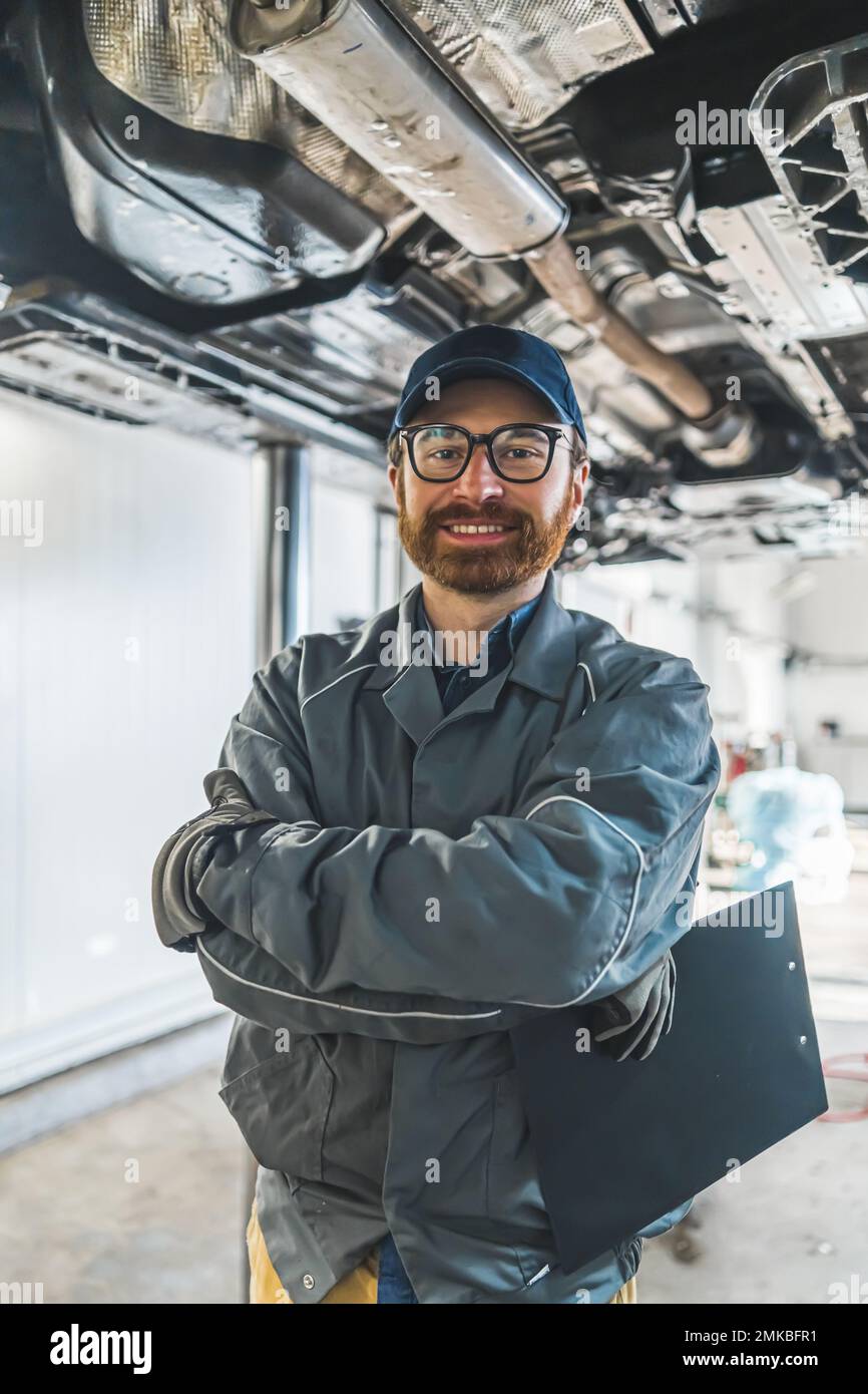 Car mechanic under a lifted vehicle with a clipboard for notes in a car ...