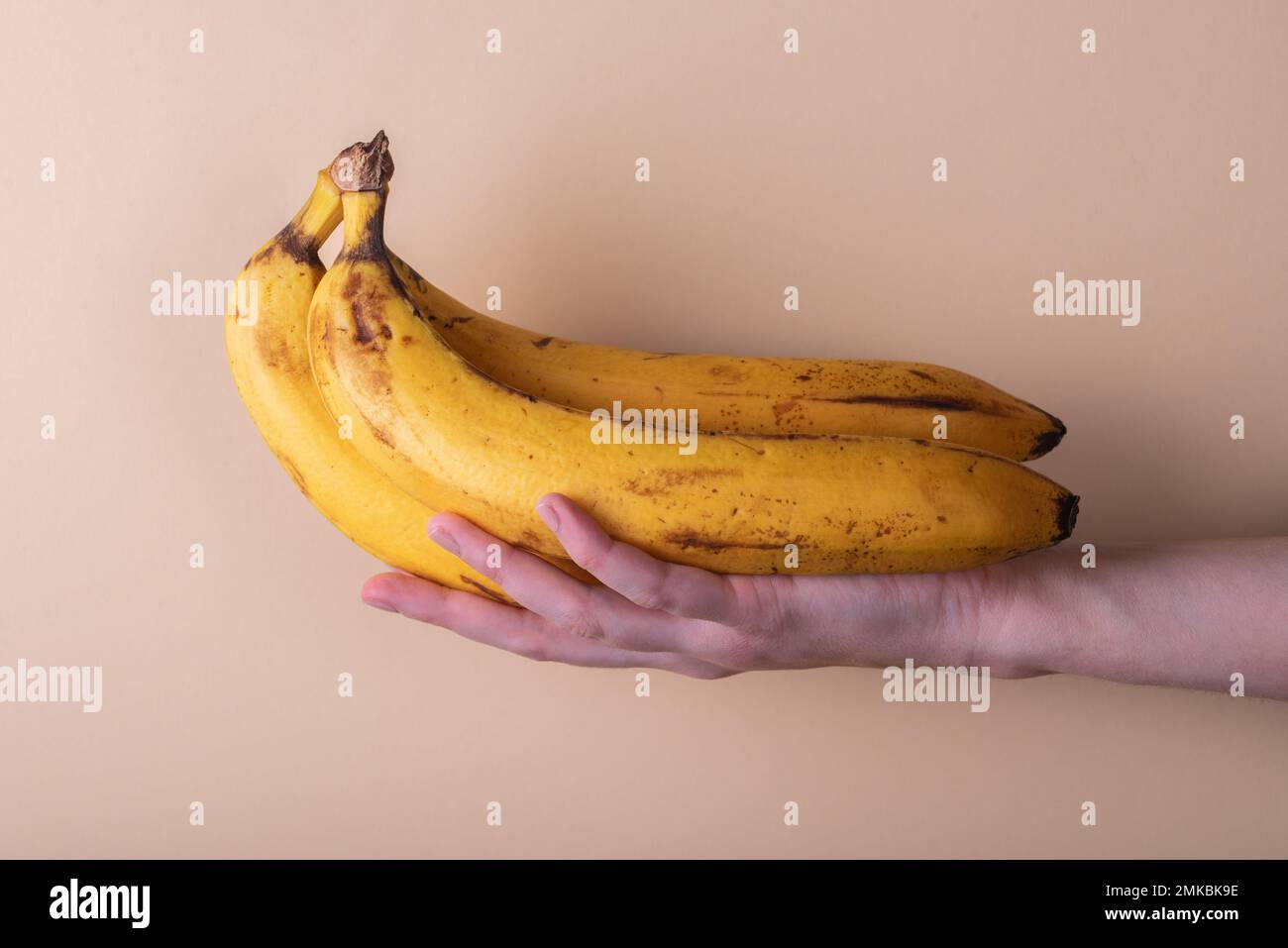Three ripe yellow bananas in woman hand on beige background. Female ...