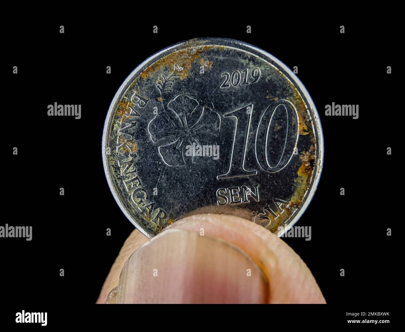 Closeup finger holding rusty old 10 cent Malaysia coin on a black ...