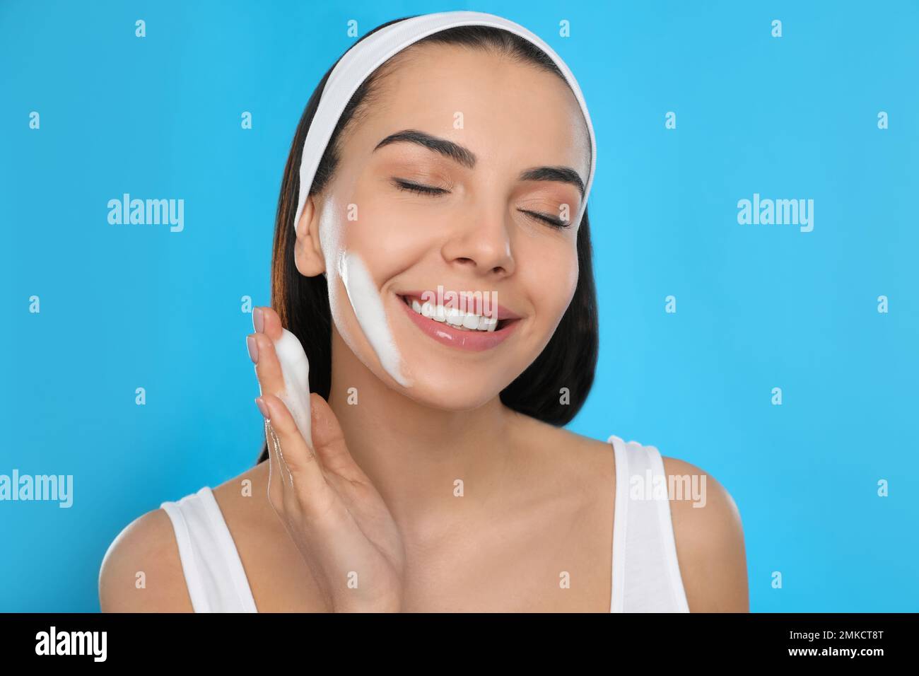 Young woman applying cosmetic product on light blue background. Washing ...