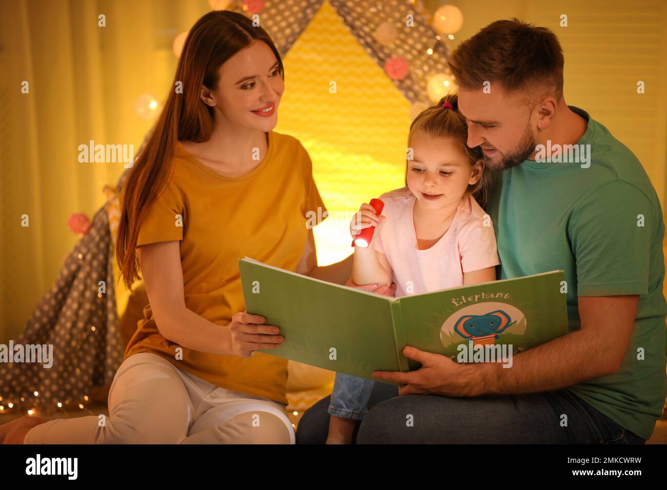 Family with flashlight reading book at home Stock Photo - Alamy