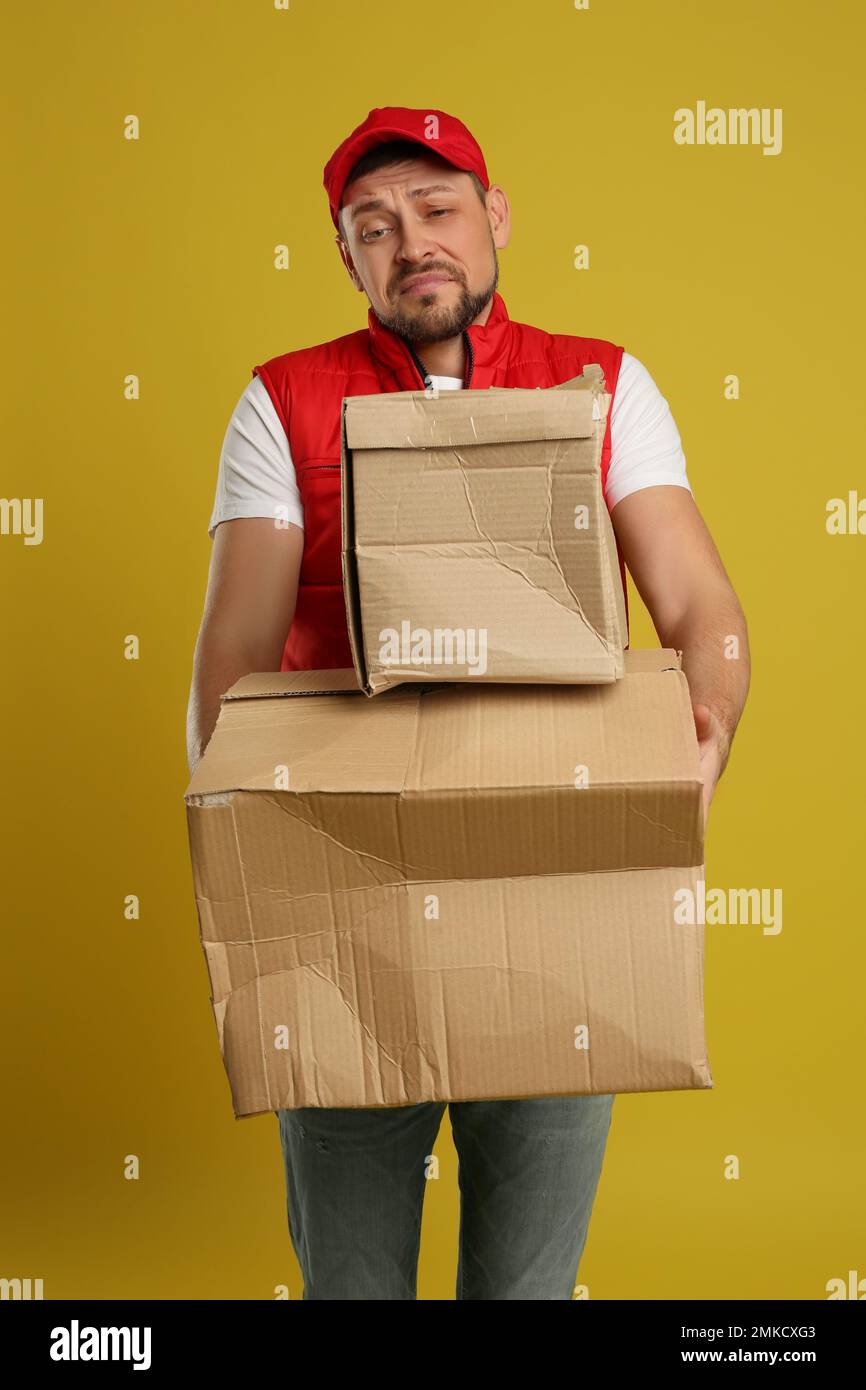 Emotional courier with damaged cardboard boxes on yellow background ...