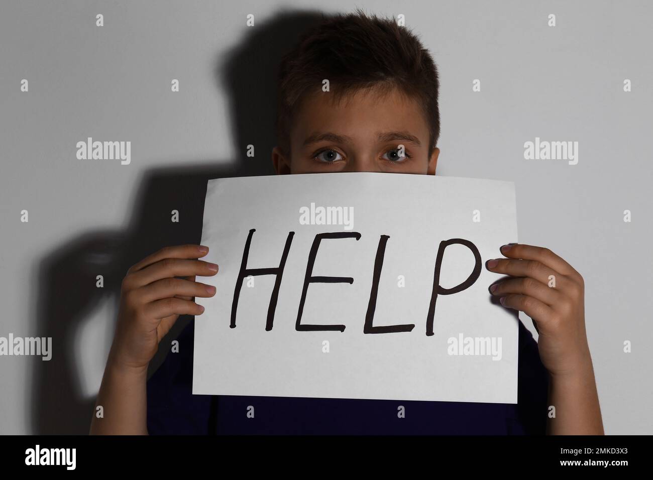 Abused little boy with sign HELP near white wall. Domestic violence ...