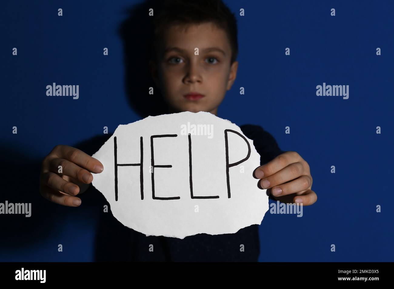 Abused little boy with sign HELP near blue wall, focus on hands ...