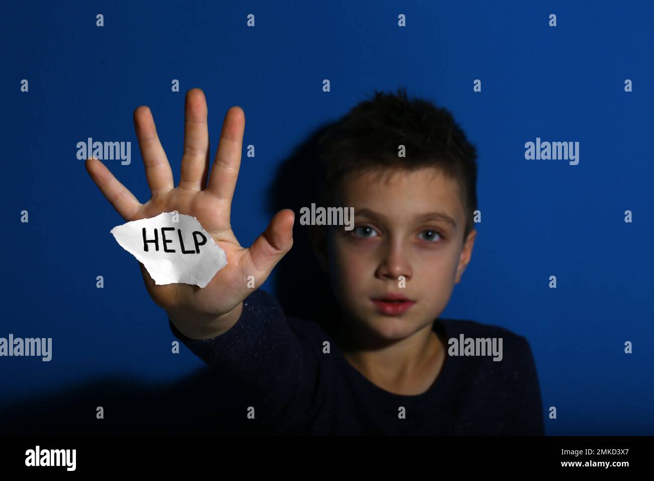 Abused little boy with sign HELP near blue wall, focus on hand ...