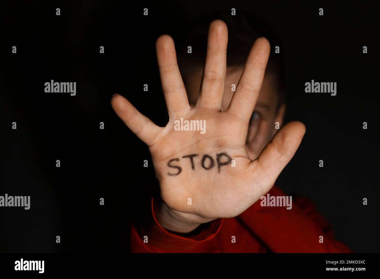 Abused little boy showing palm with word STOP against black background ...