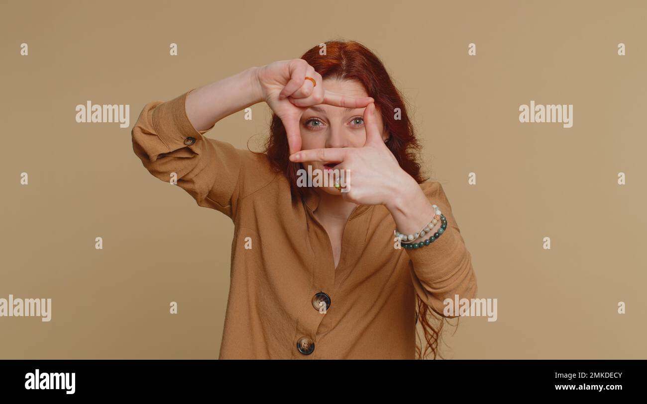 Redhead woman photographer gesturing picture frame with hands, looks ...
