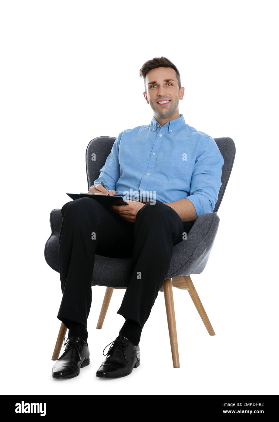 Handsome young man with clipboard sitting in armchair on white ...