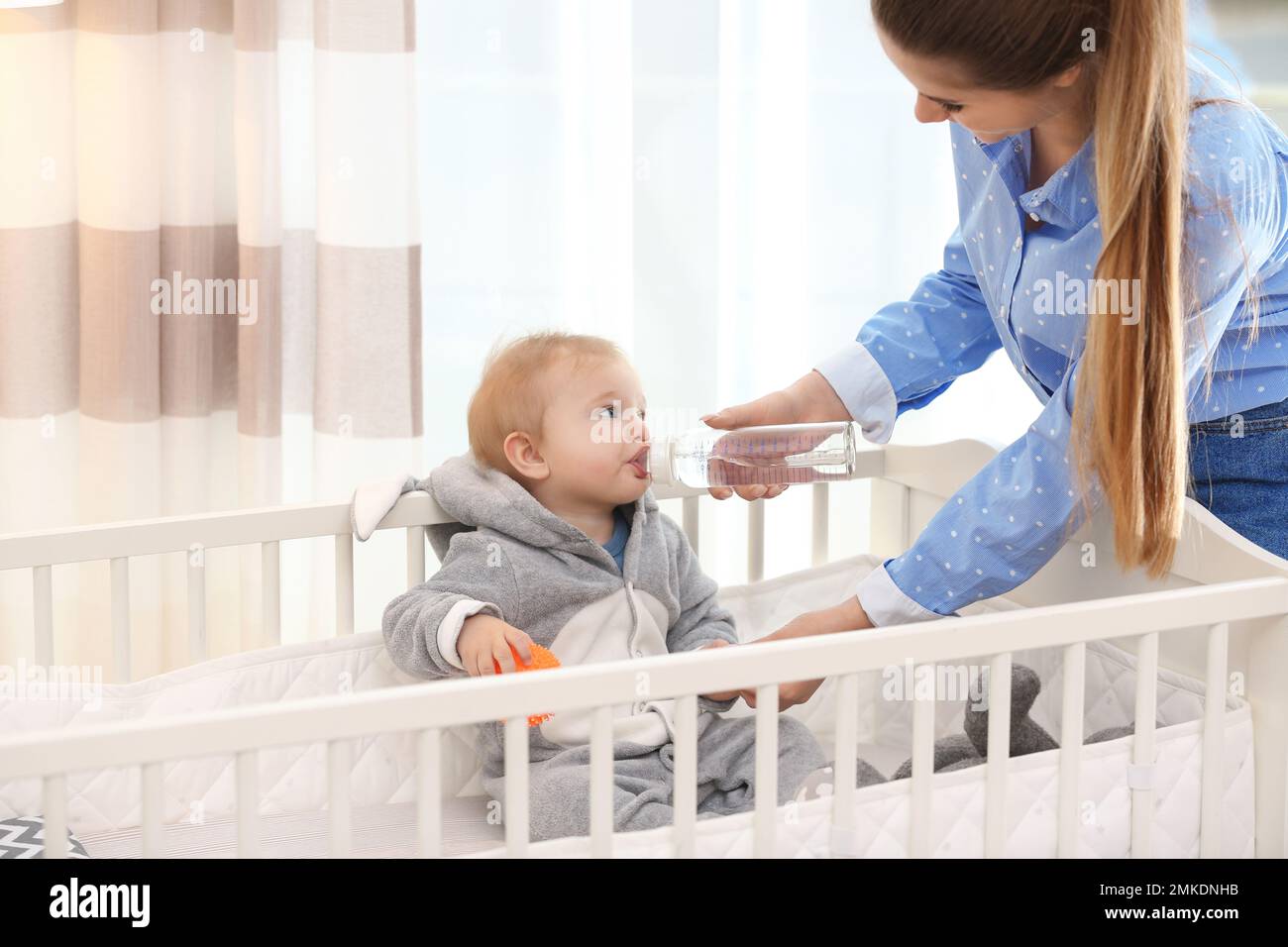 Teen nanny giving cute little baby water from bottle at home Stock ...