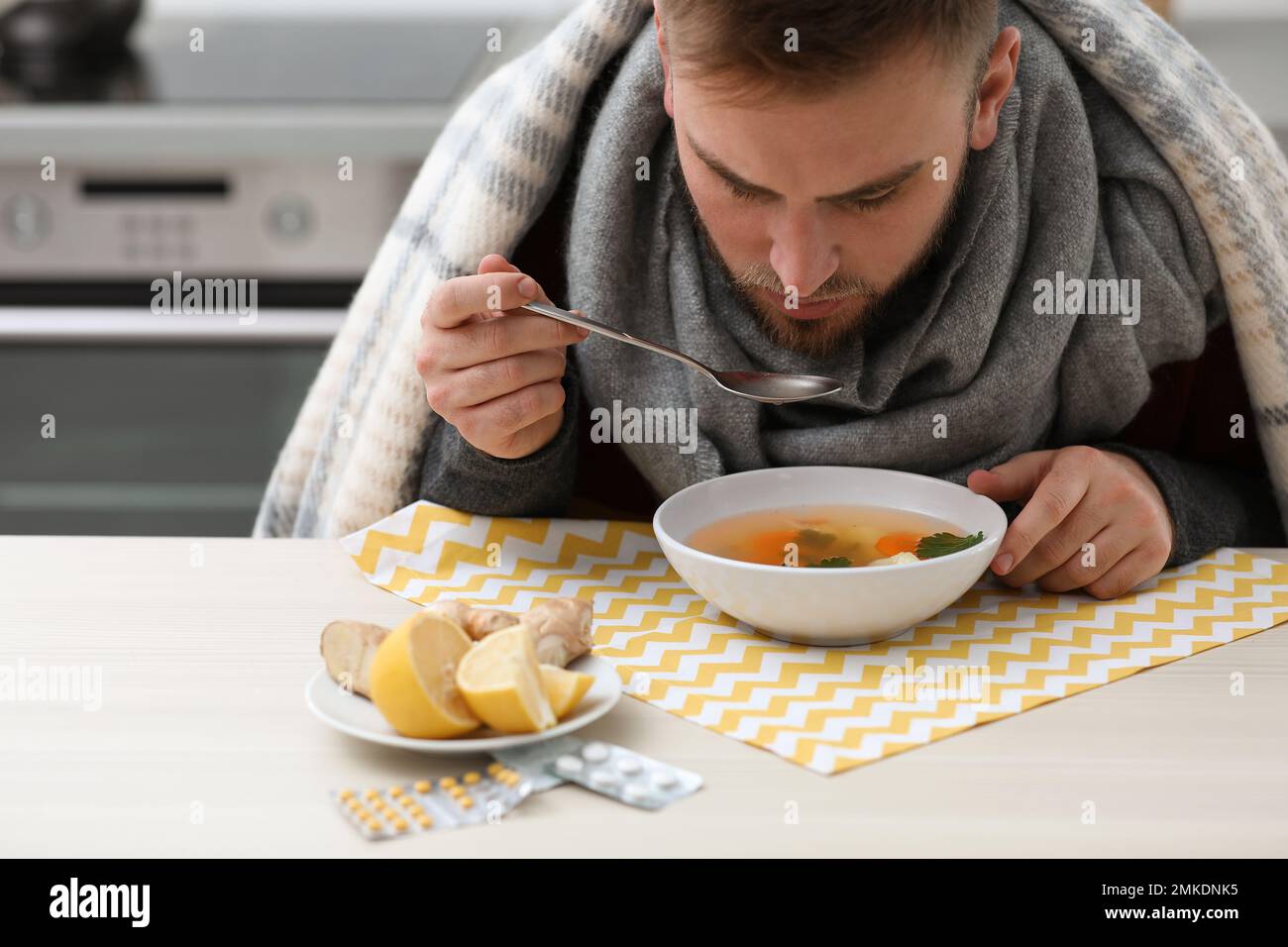 Sick young man eating tasty soup to cure flu at table in kitchen Stock ...