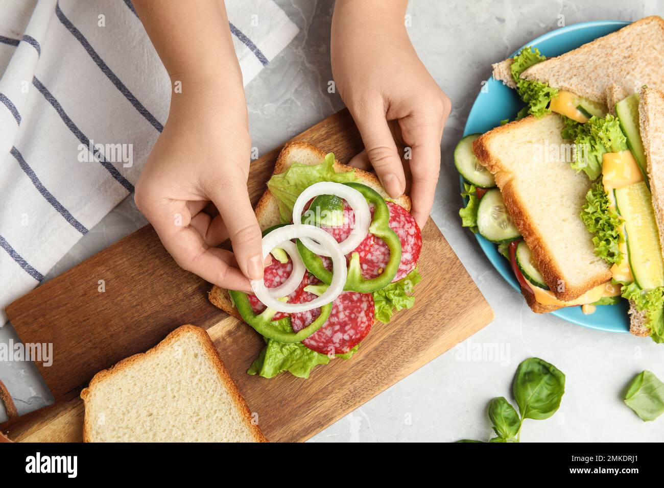 Woman adding onion to tasty sandwich at light grey marble table, top ...
