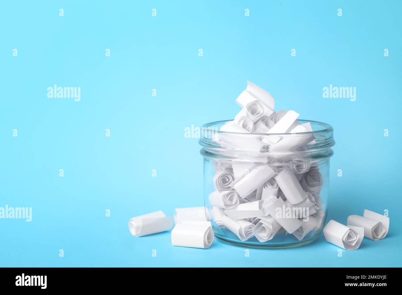 Glass jar full of rolled paper sheets on light blue background, space ...