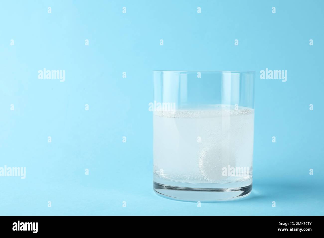 Glass of water with effervescent tablet on light blue background, space ...