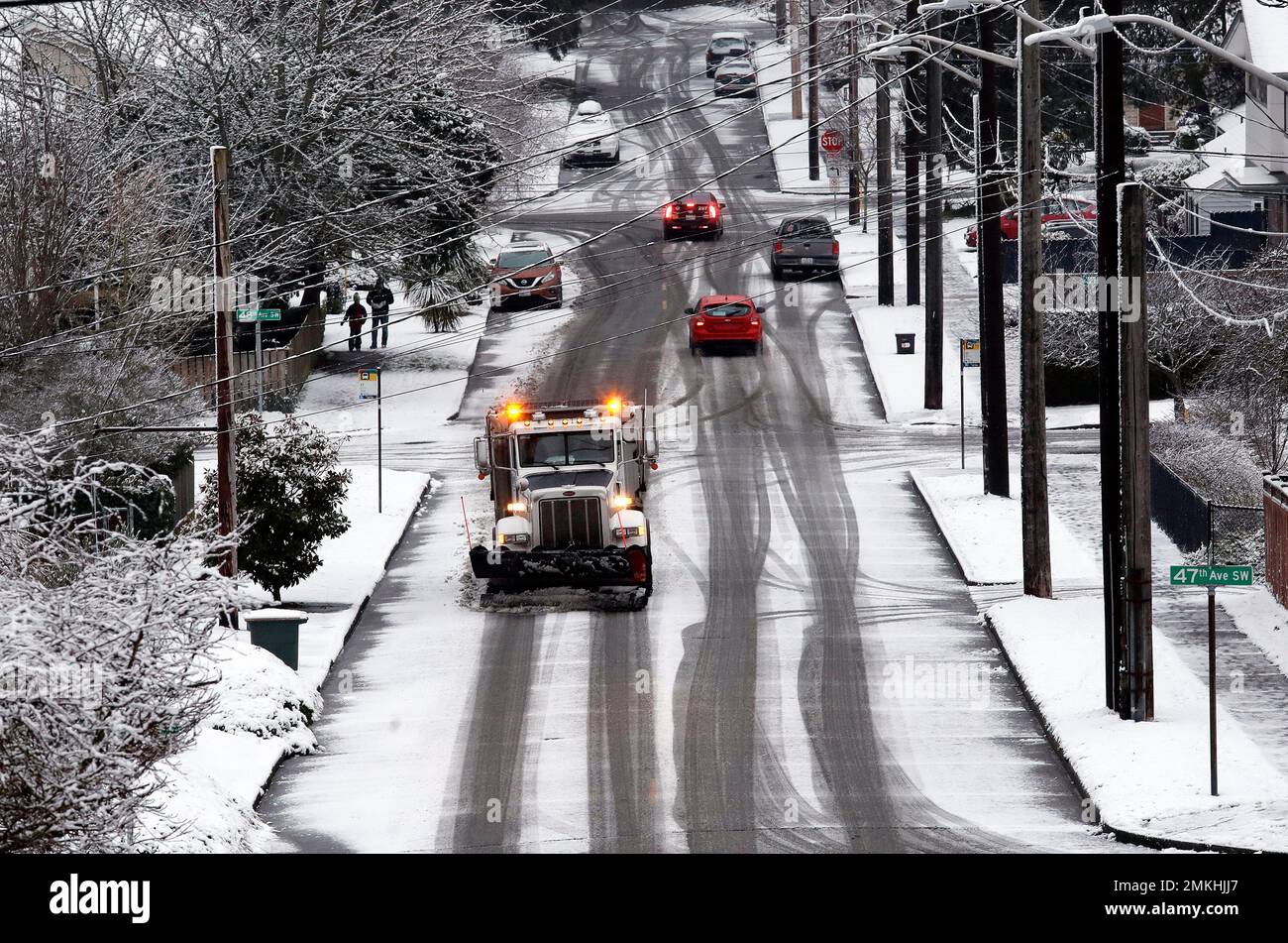 A city snowplow makes its way up a residential street early in a ...
