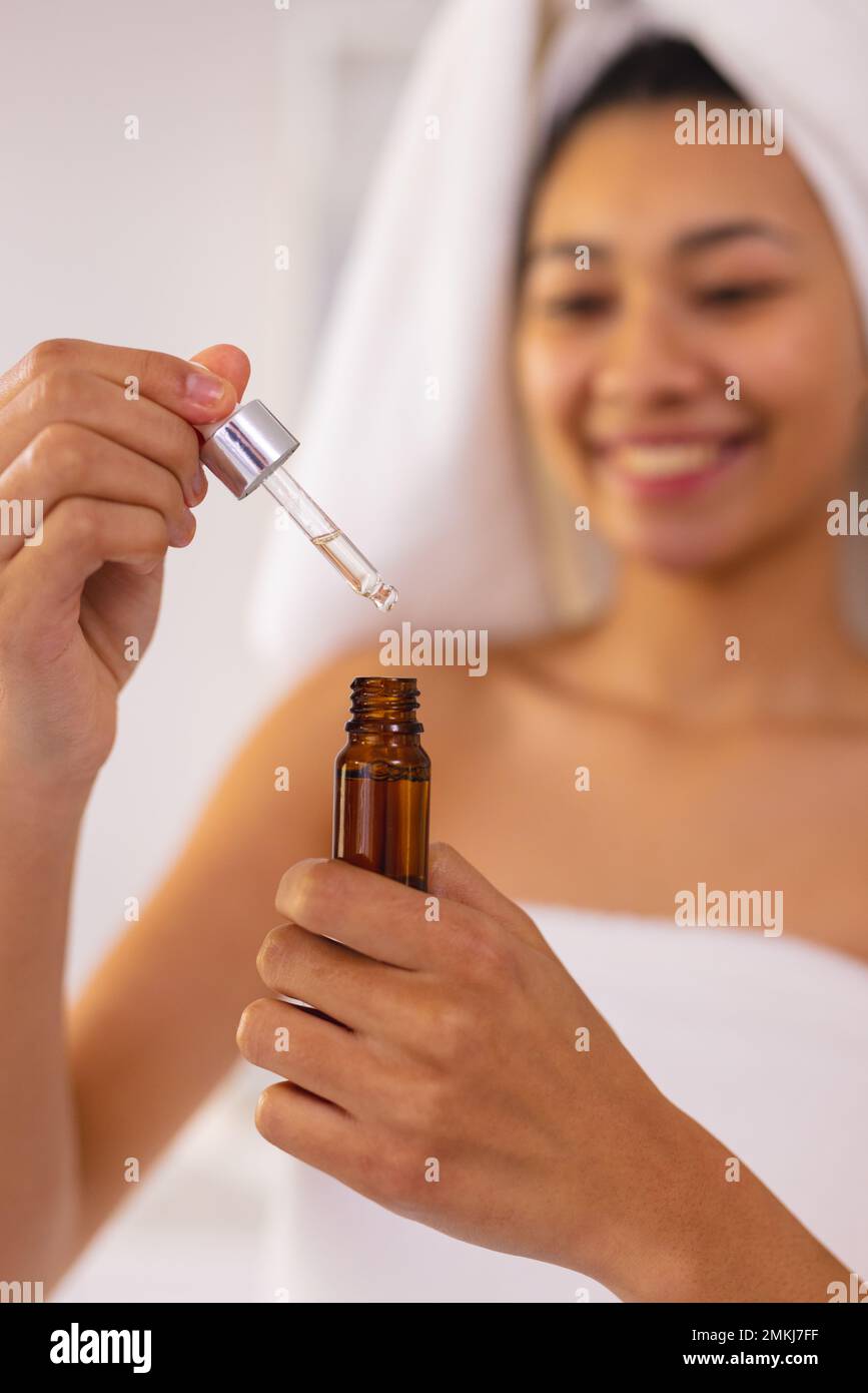 Vertical of smiling biracial woman in bathroom, holding essential oil ...