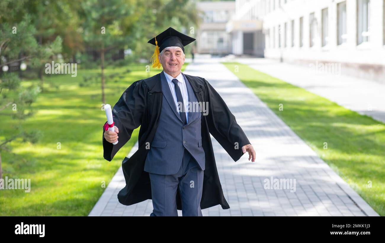 An old man in a graduation gown walks outdoors and holds a diploma ...