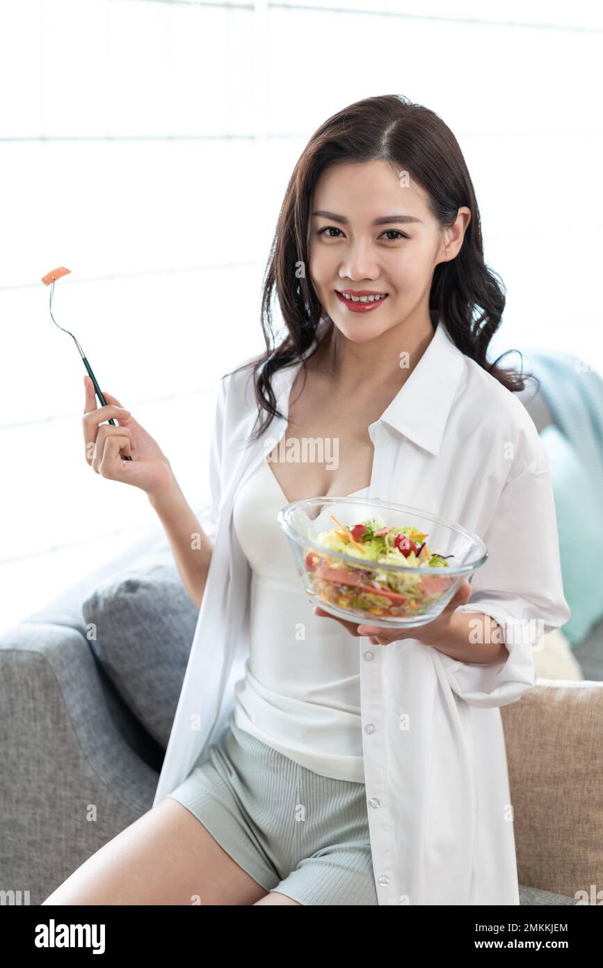 Young woman sitting on the sofa eating salad Stock Photo - Alamy