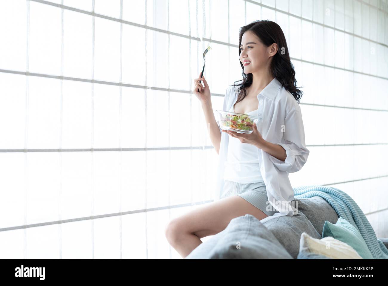 A young woman sit by the window eating salad Stock Photo - Alamy